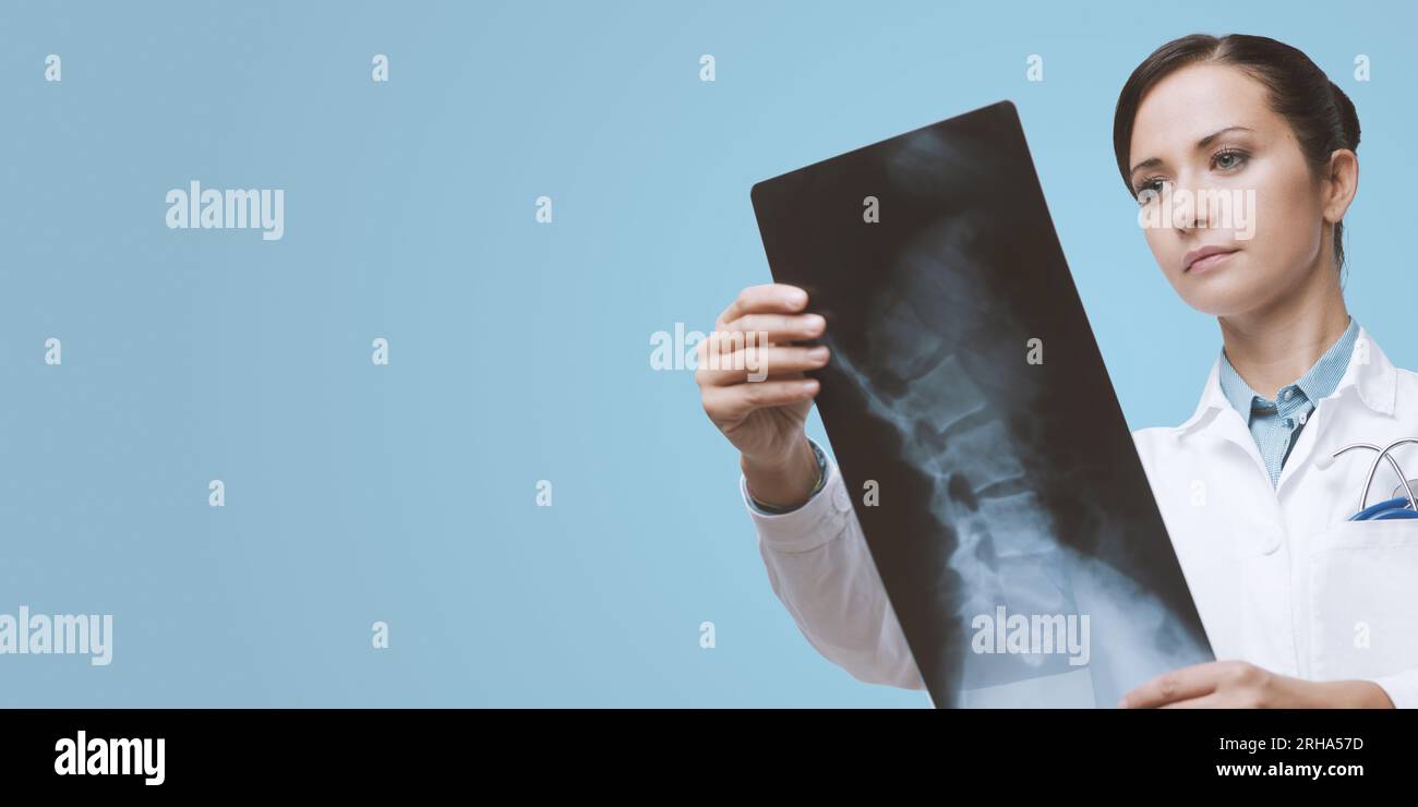 Confident female radiologist checking x-ray image of spinal column ...
