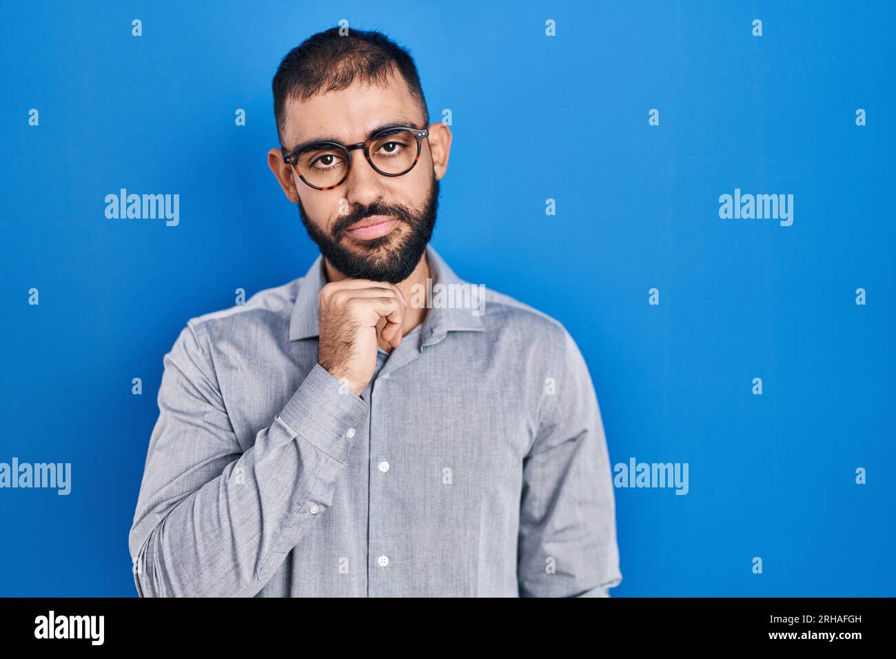 Middle east man with beard standing over blue background with hand on ...