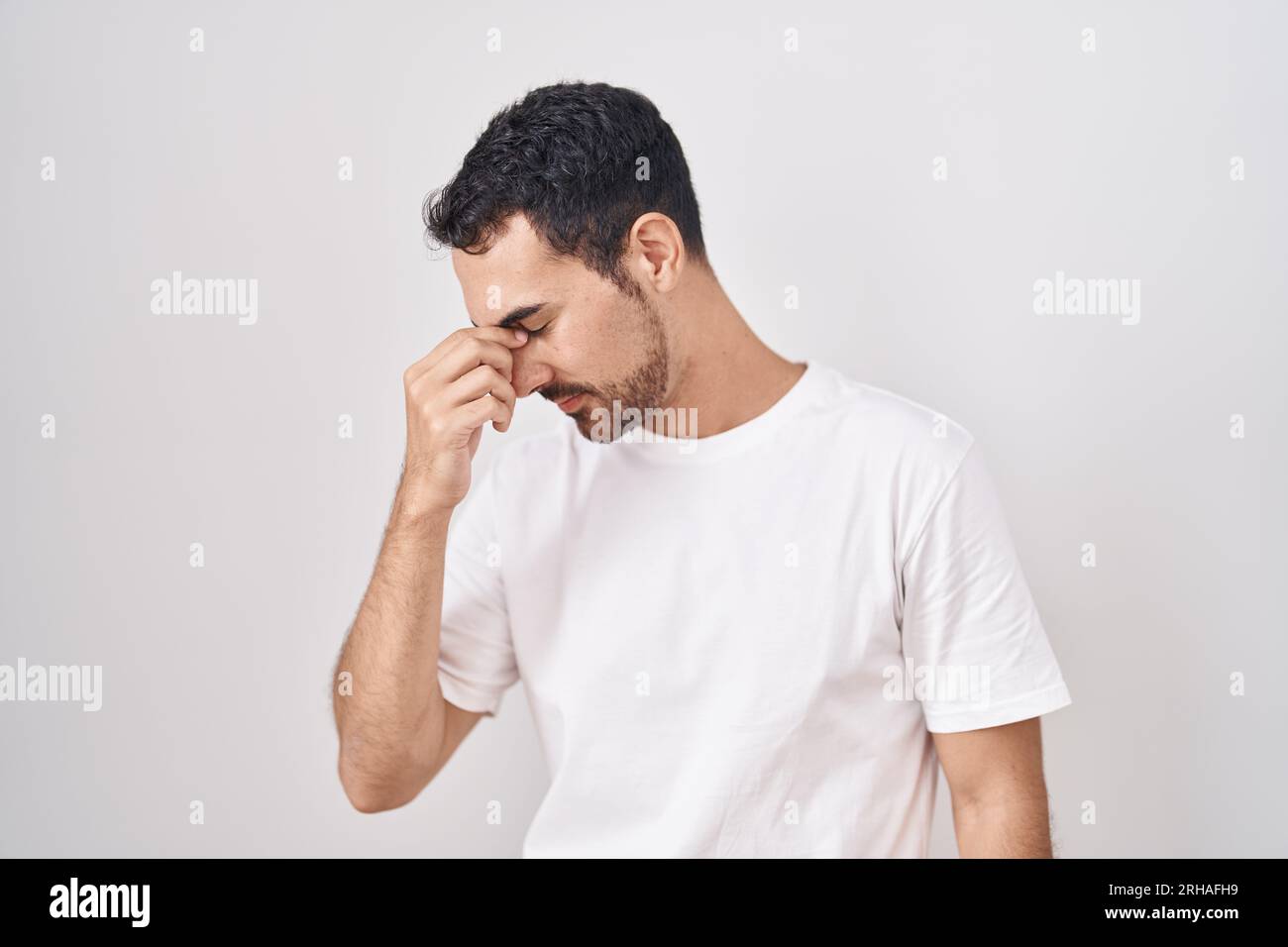 Handsome hispanic man standing over white background tired rubbing nose ...