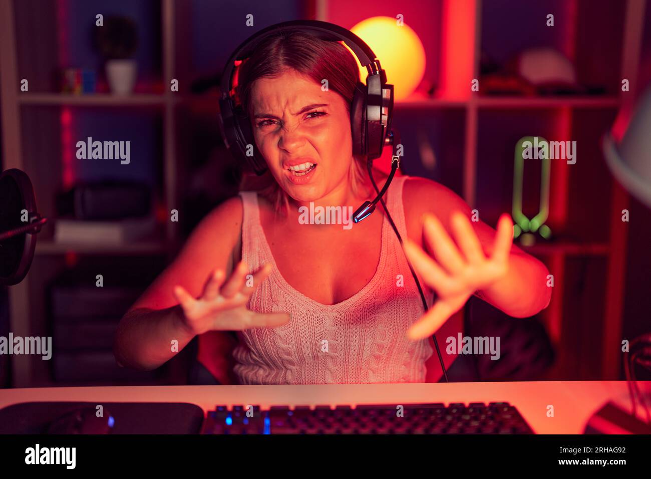 Young blonde woman playing video games wearing headphones afraid and ...