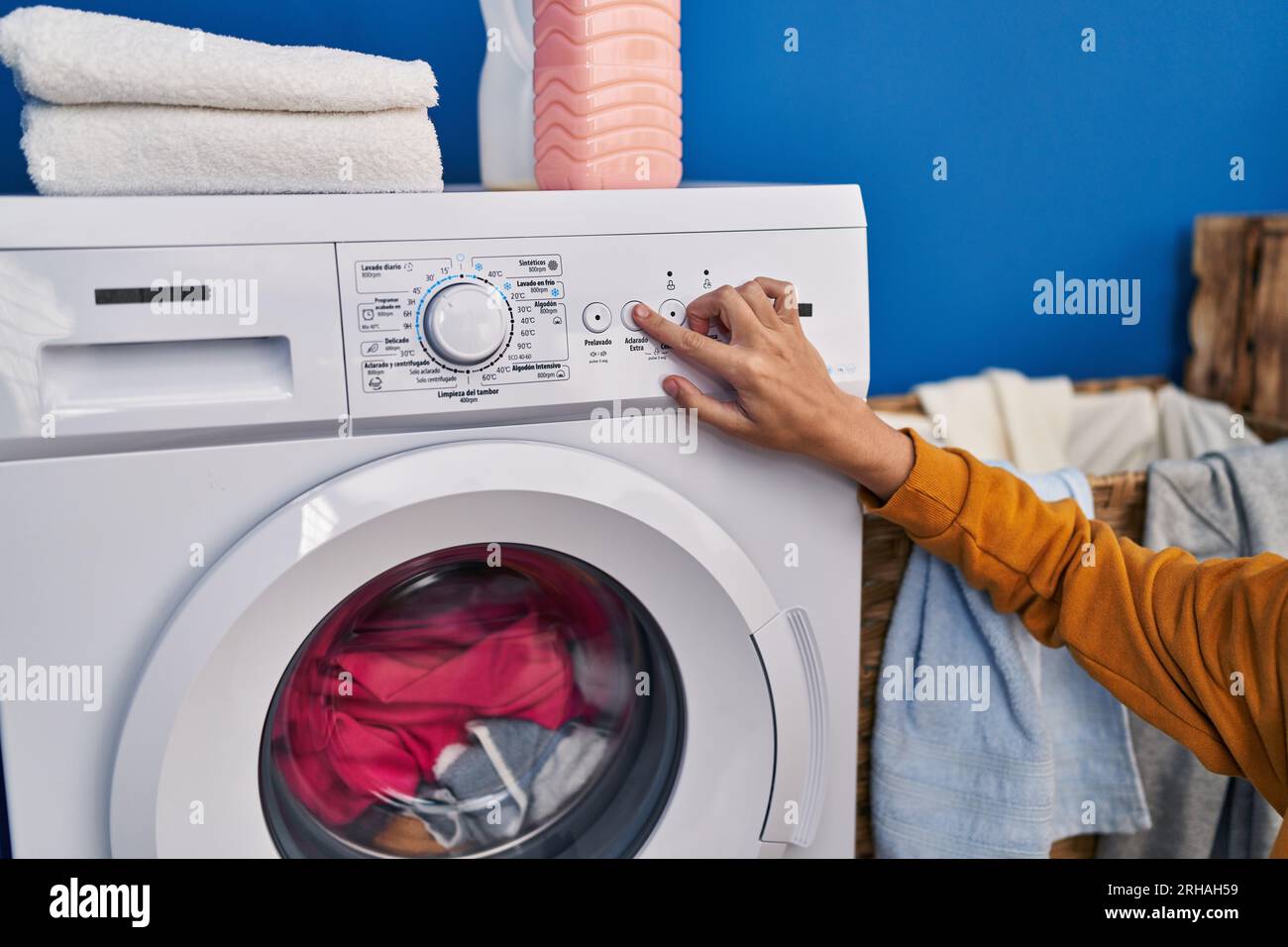 Young blonde woman sitting on floor turning washing machine on at ...