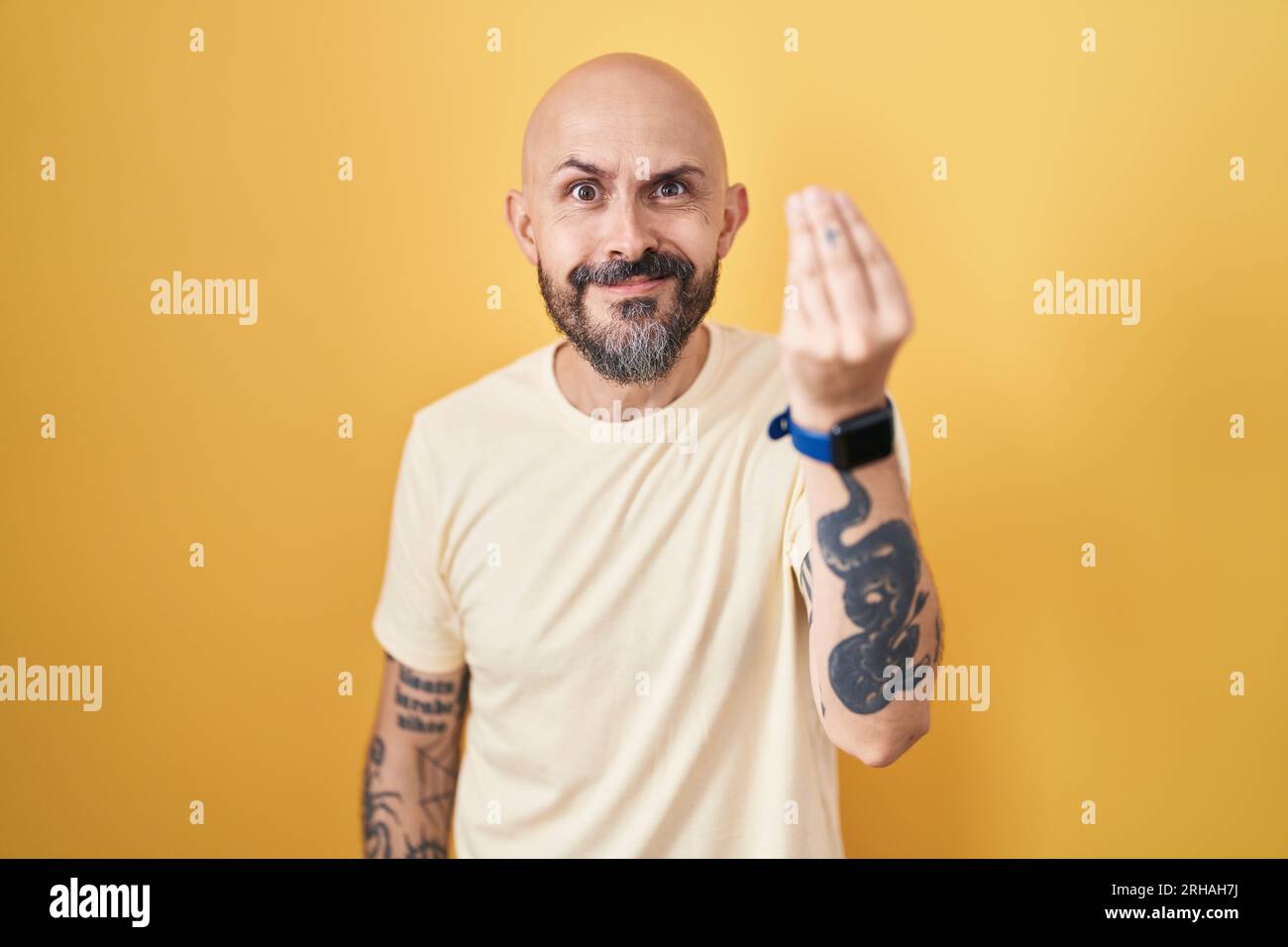 Hispanic man with tattoos standing over yellow background doing italian ...