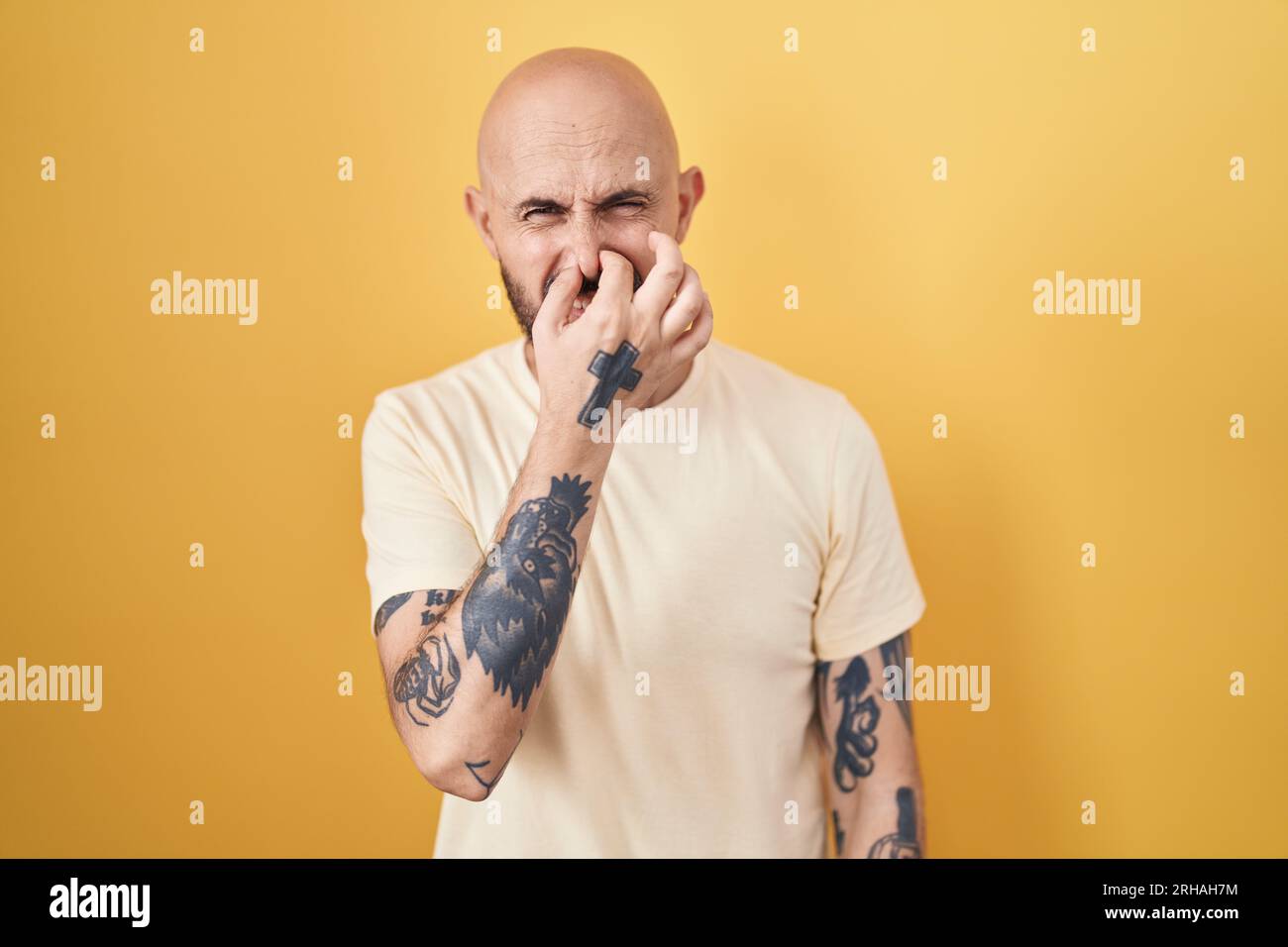 Hispanic man with tattoos standing over yellow background smelling ...
