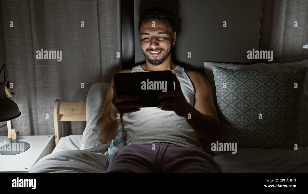 Young arab man watching video on touchpad sitting on bed at bedroom Stock Photo - Alamy