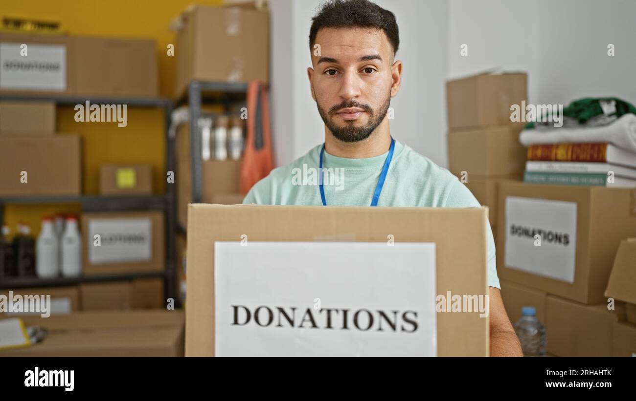 Young arab man volunteer holding donations package at charity center ...