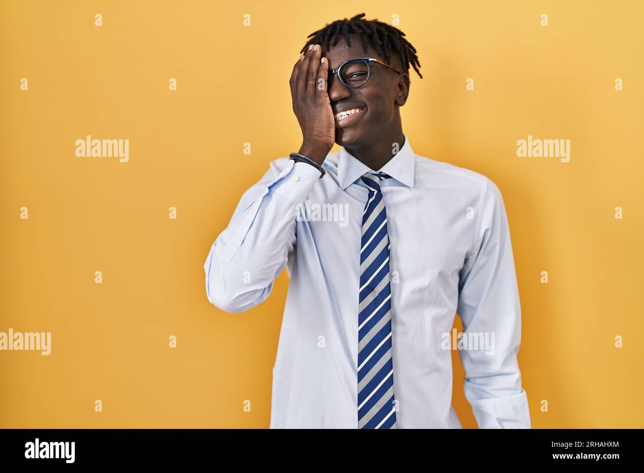 African man with dreadlocks standing over yellow background covering ...