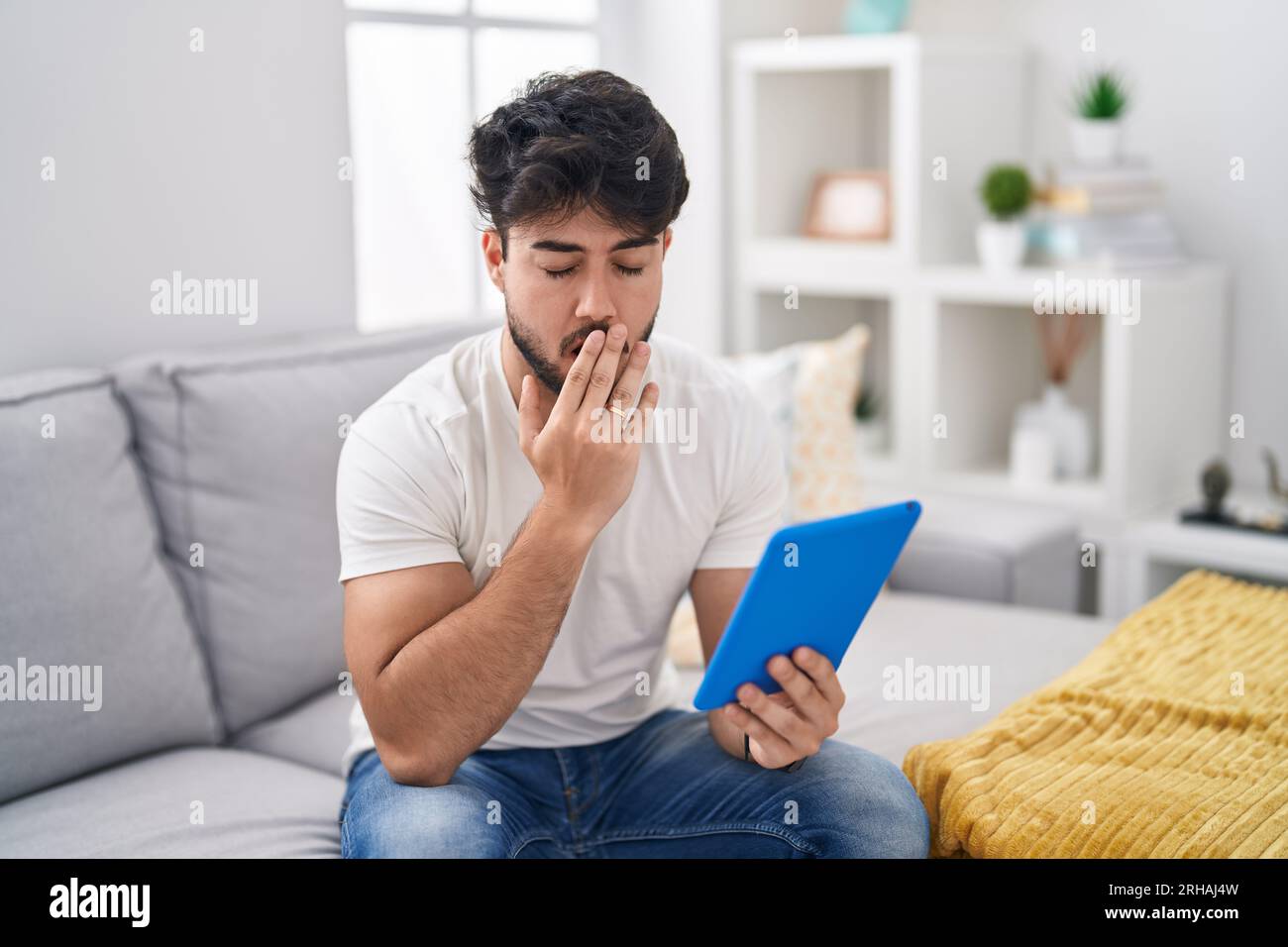 Hispanic man with beard using touchpad sitting on the sofa bored ...