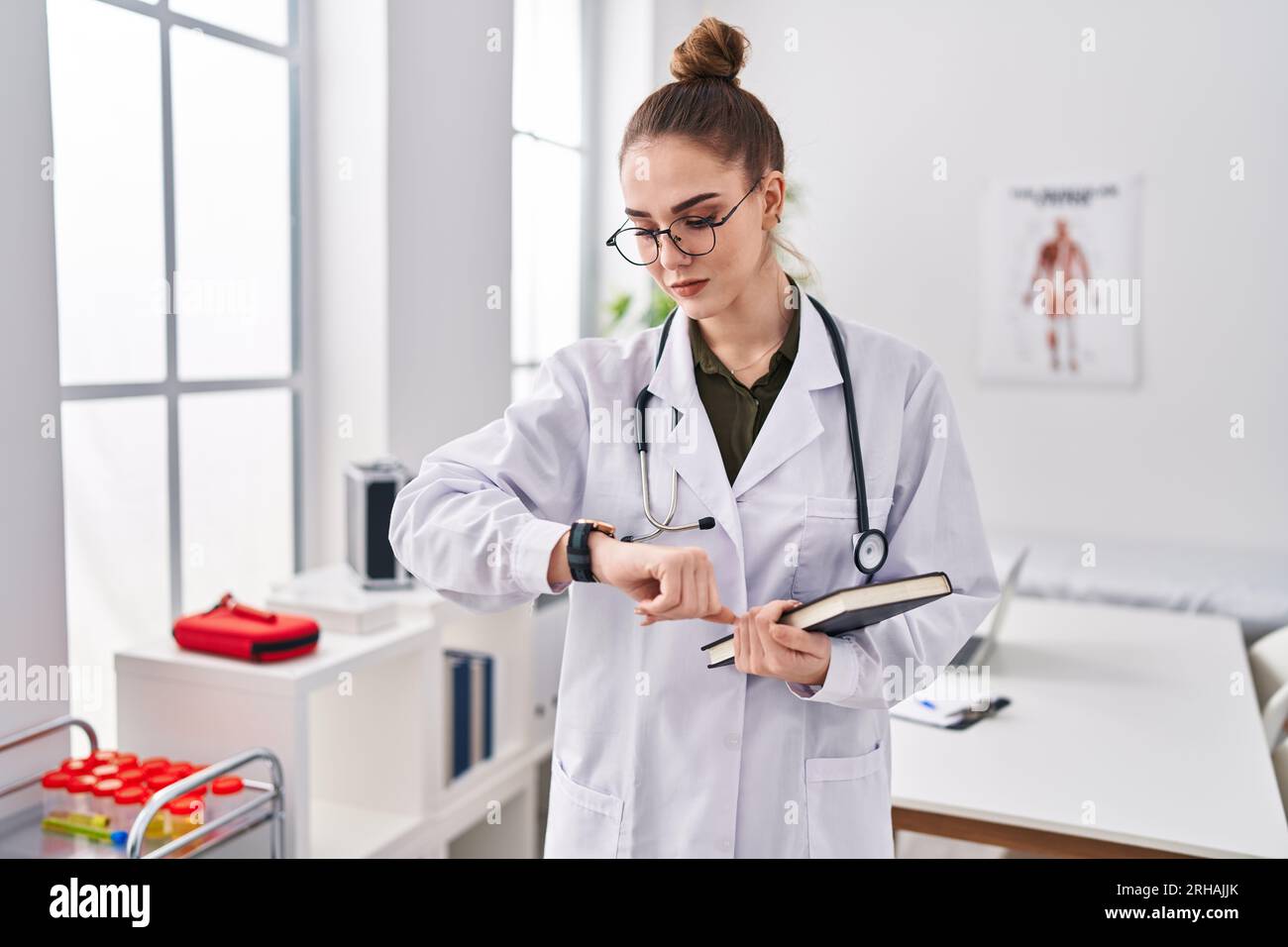 Young woman wearing doctor uniform looking watch at clinic Stock Photo ...