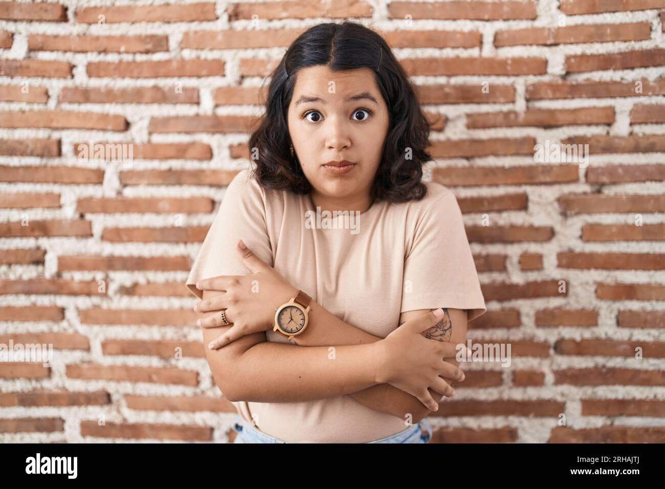 Young hispanic woman standing over bricks wall shaking and freezing for ...