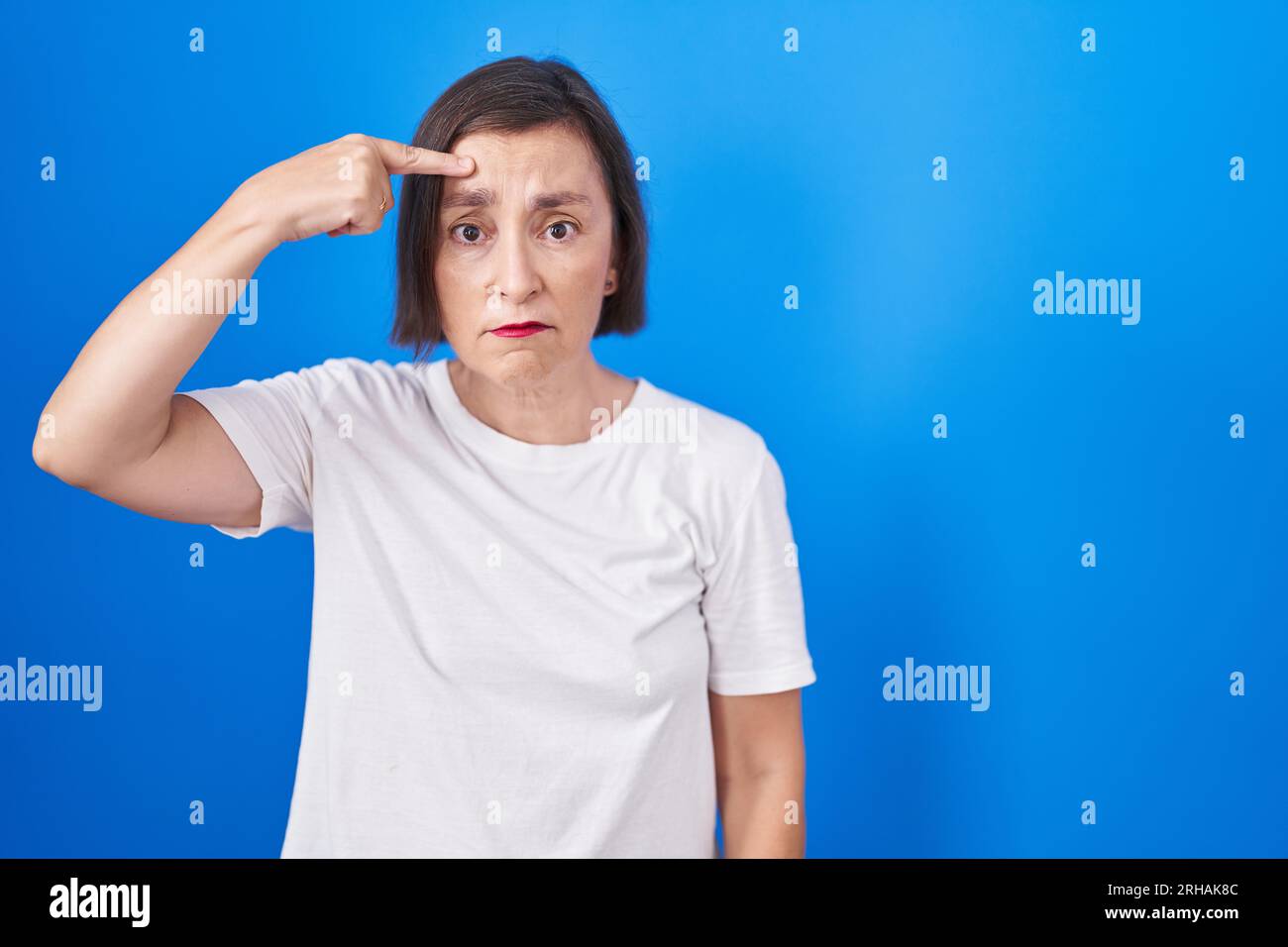 Middle age hispanic woman standing over blue background pointing ...