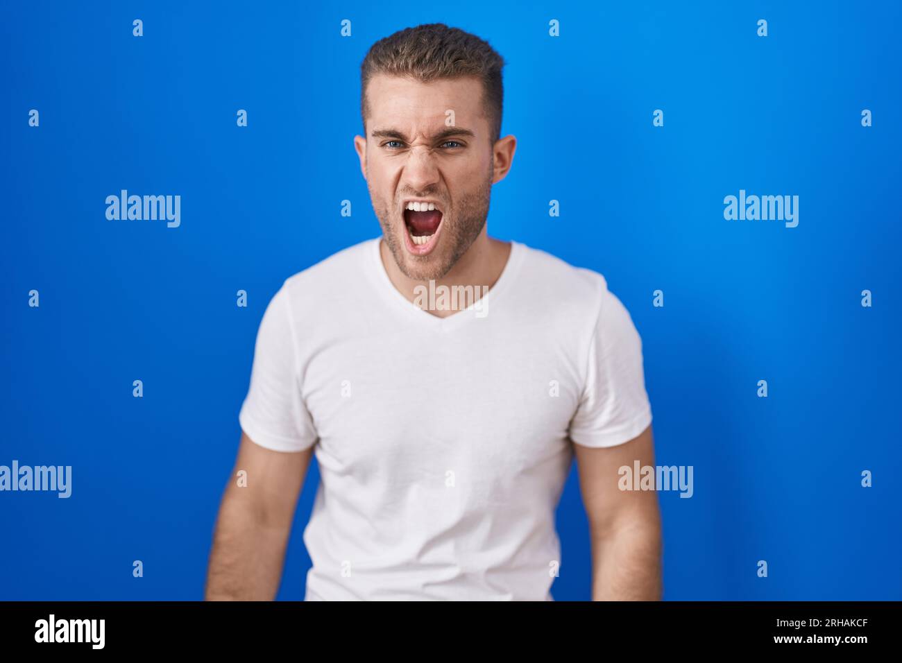 Young caucasian man standing over blue background angry and mad ...