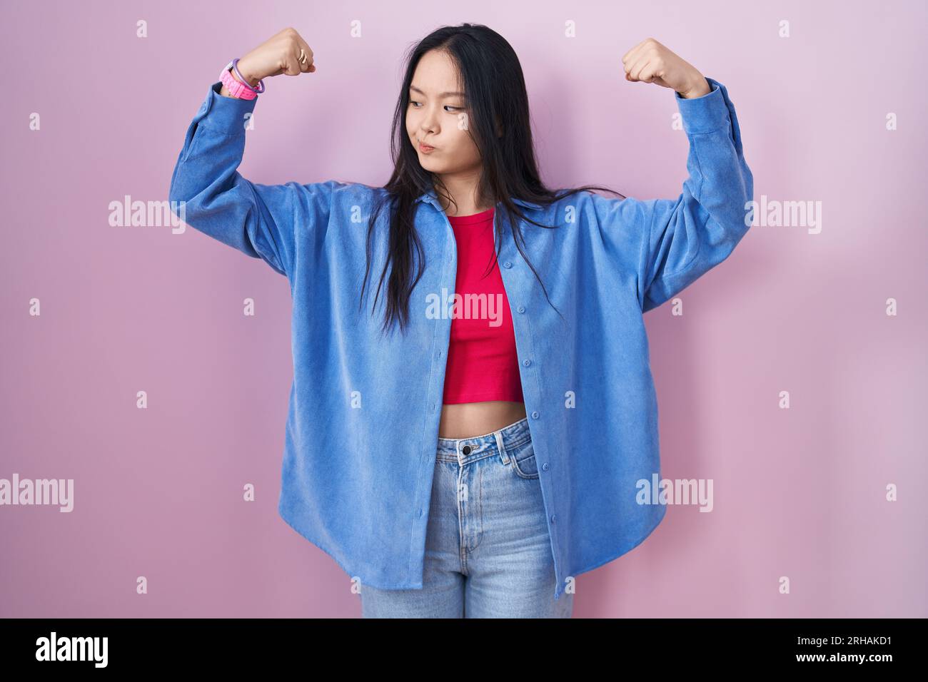 Young asian woman standing over pink background showing arms muscles ...