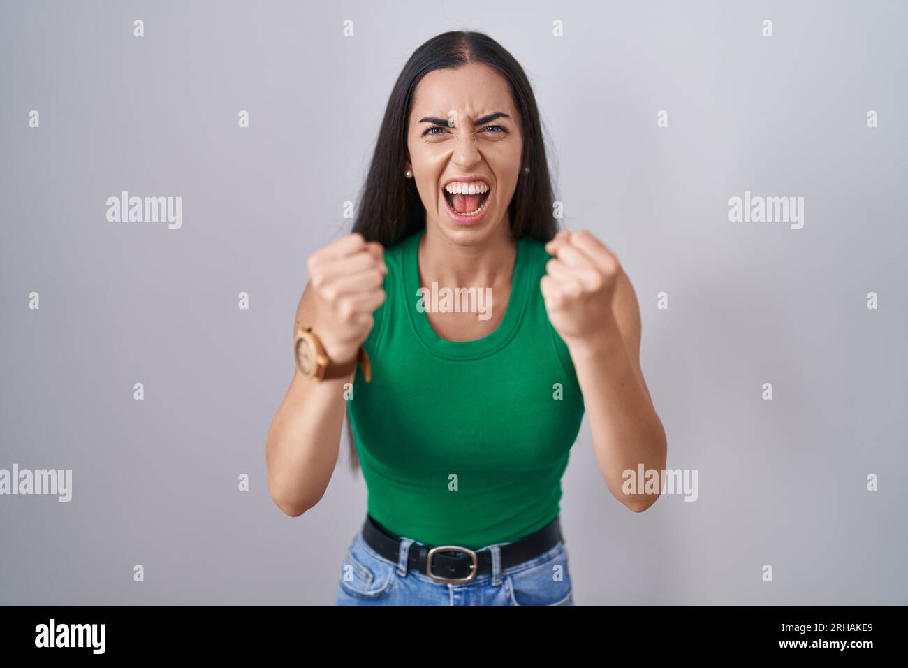Young woman standing over isolated background angry and mad raising ...