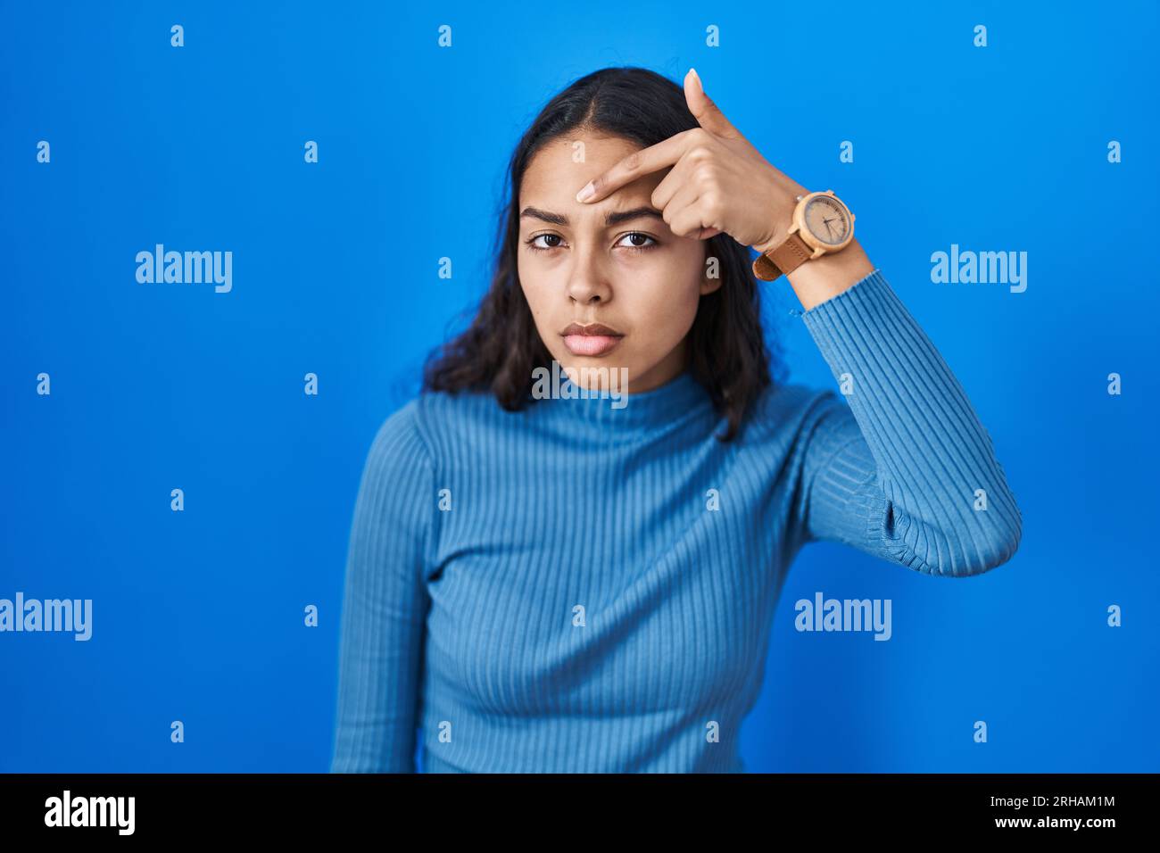 Young brazilian woman standing over blue isolated background pointing ...