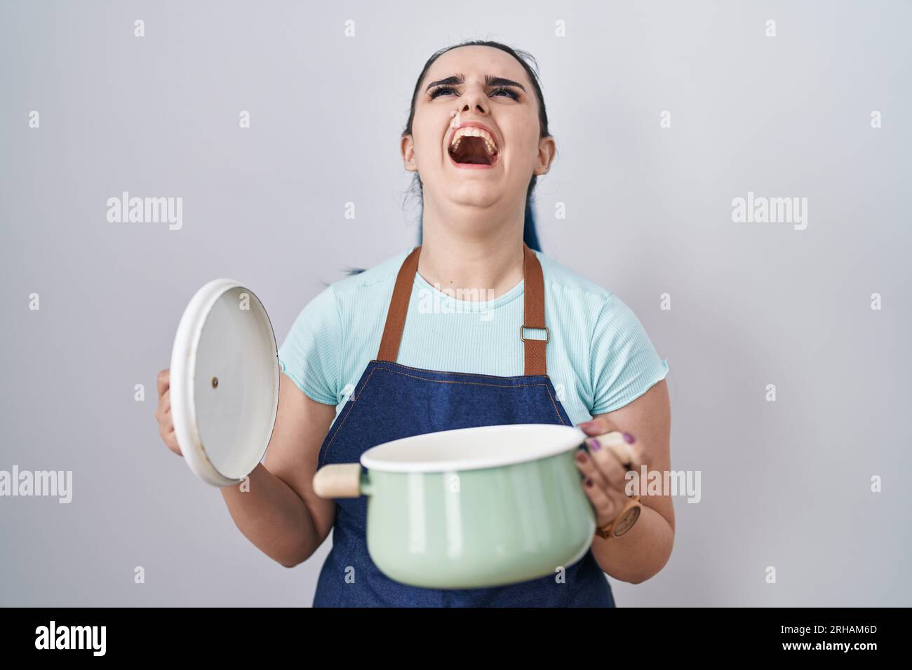 Young modern girl with blue hair wearing apron holding cooking pot ...