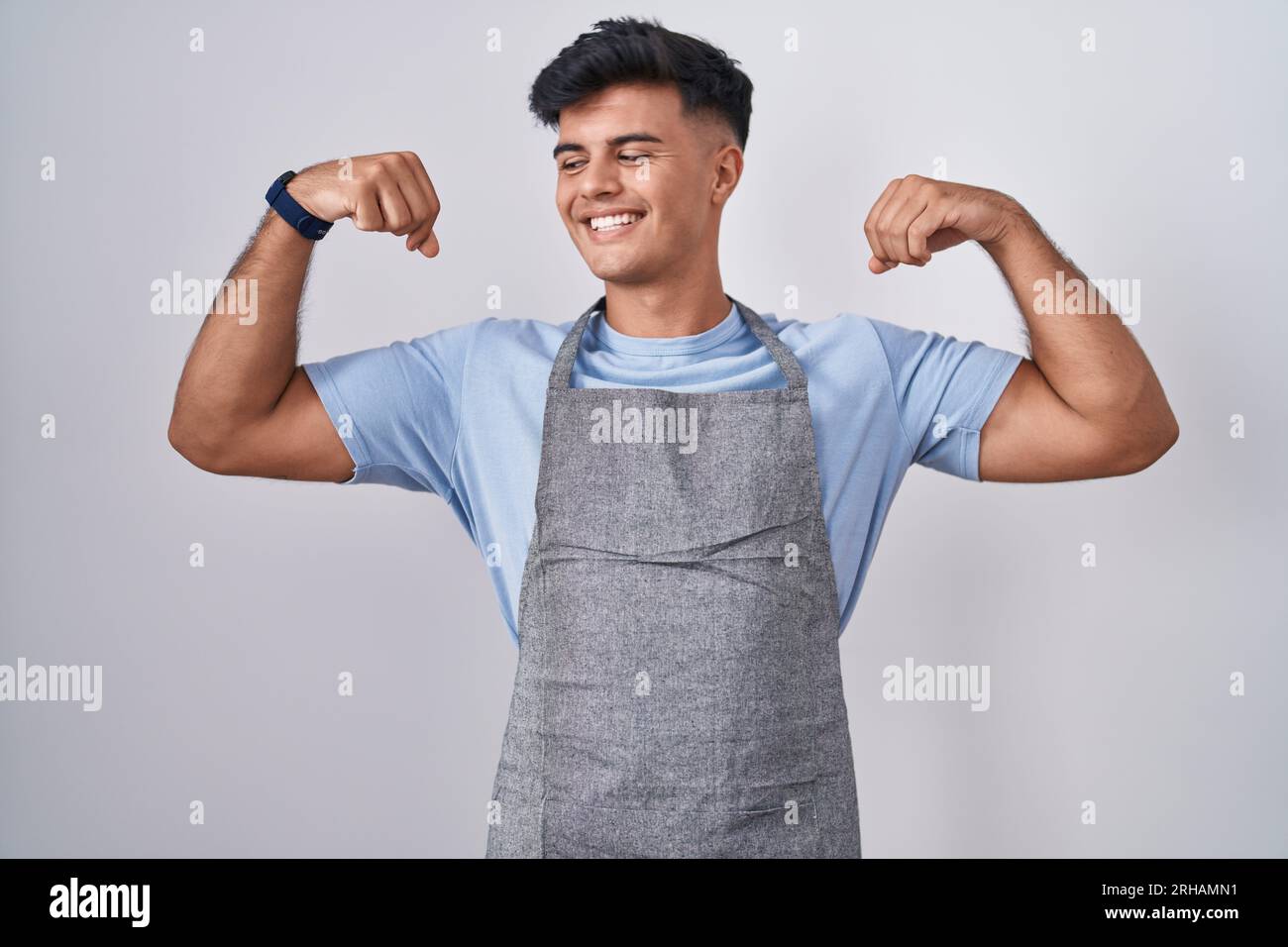 Hispanic young man wearing apron over white background showing arms ...