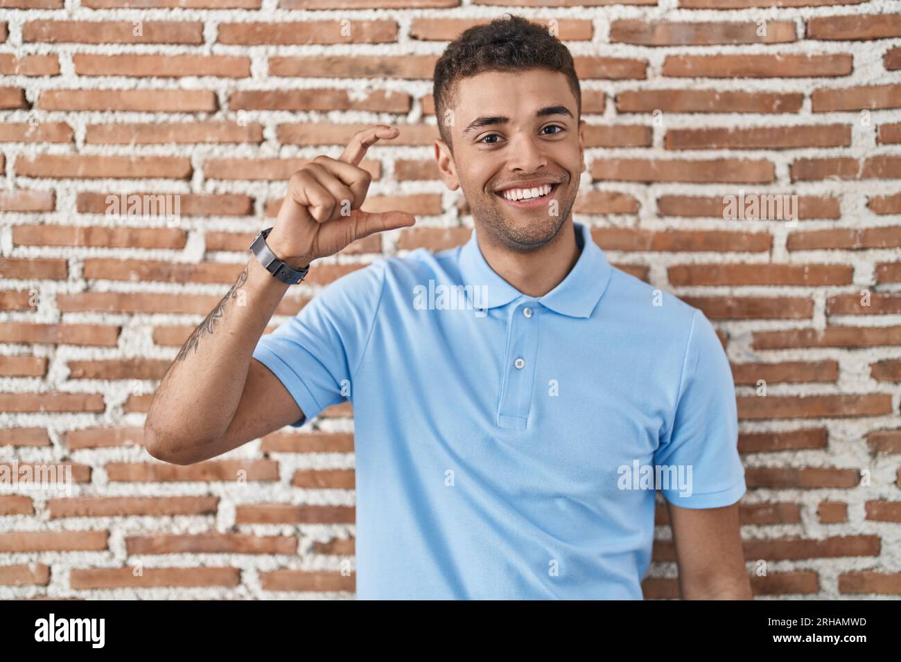 Brazilian young man standing over brick wall smiling and confident ...