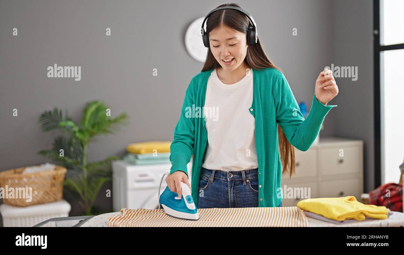Young chinese woman listening to music ironing clothes dancing at ...