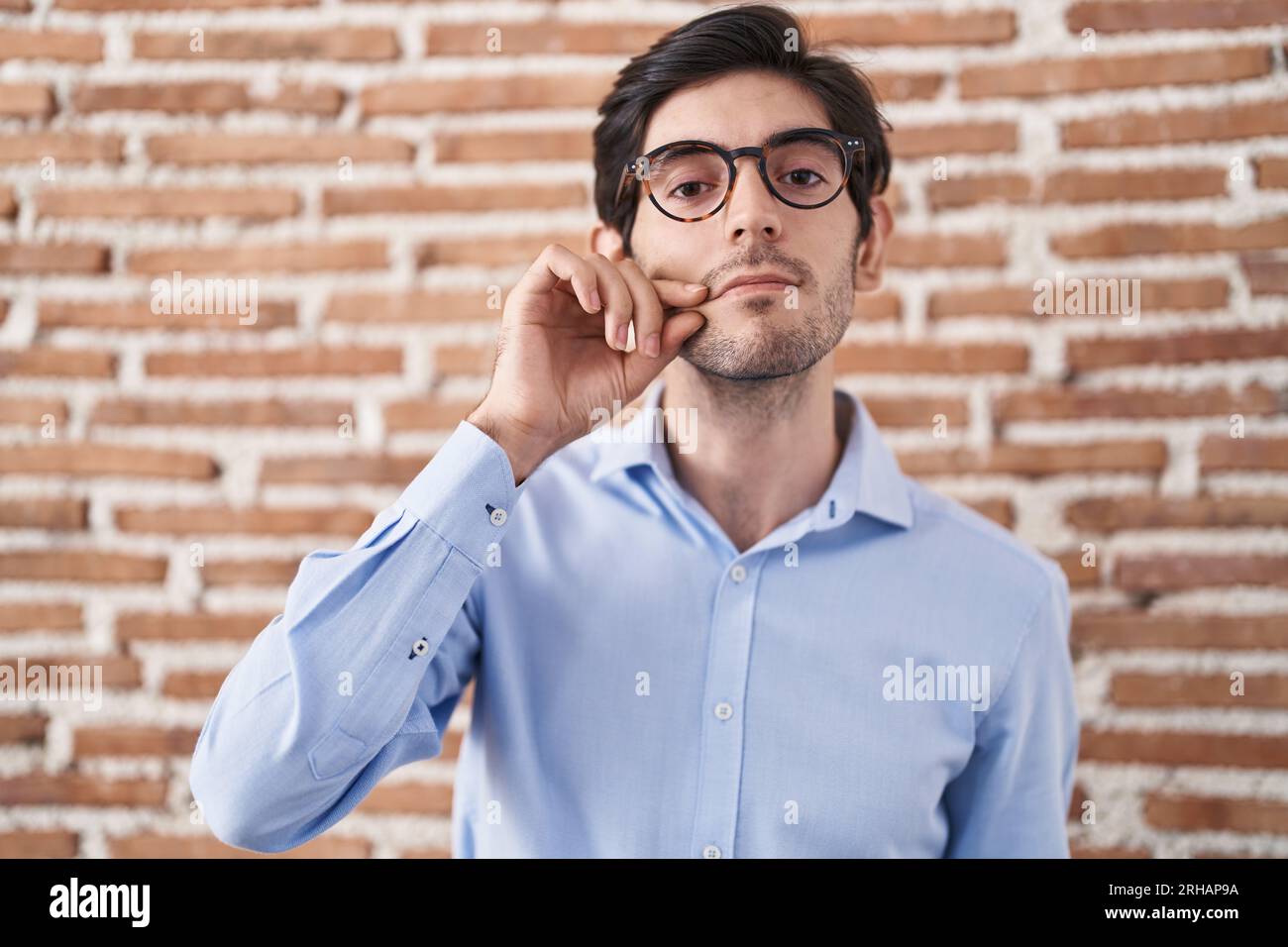 Young hispanic man standing over brick wall background mouth and lips ...
