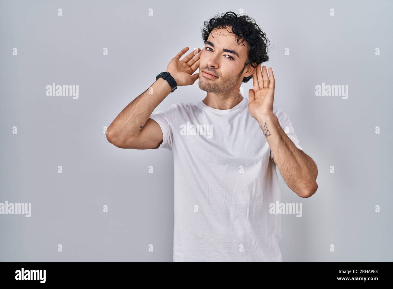 Hispanic man standing over isolated background trying to hear both ...