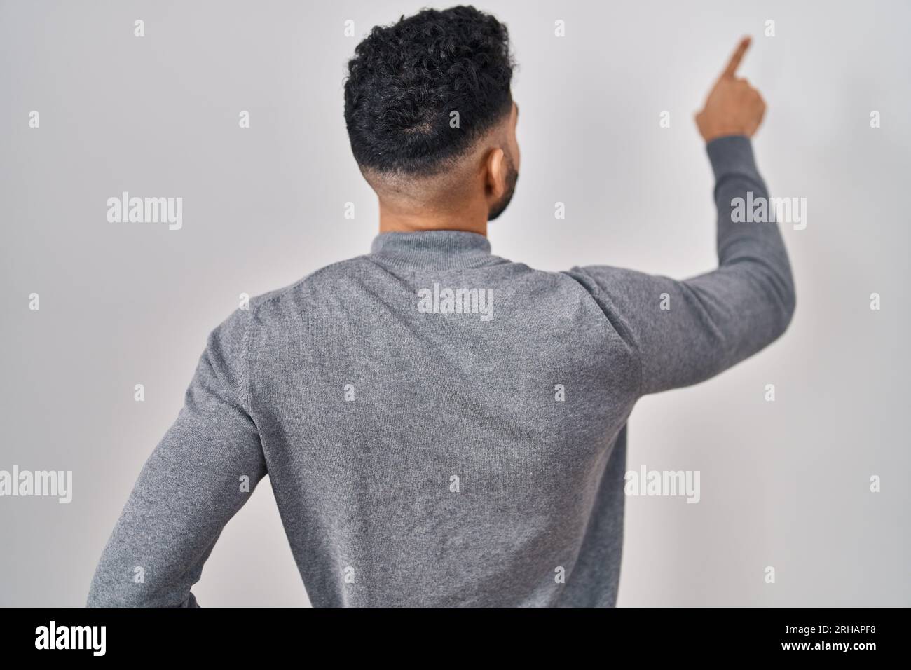 Hispanic man with beard standing over white background posing backwards ...