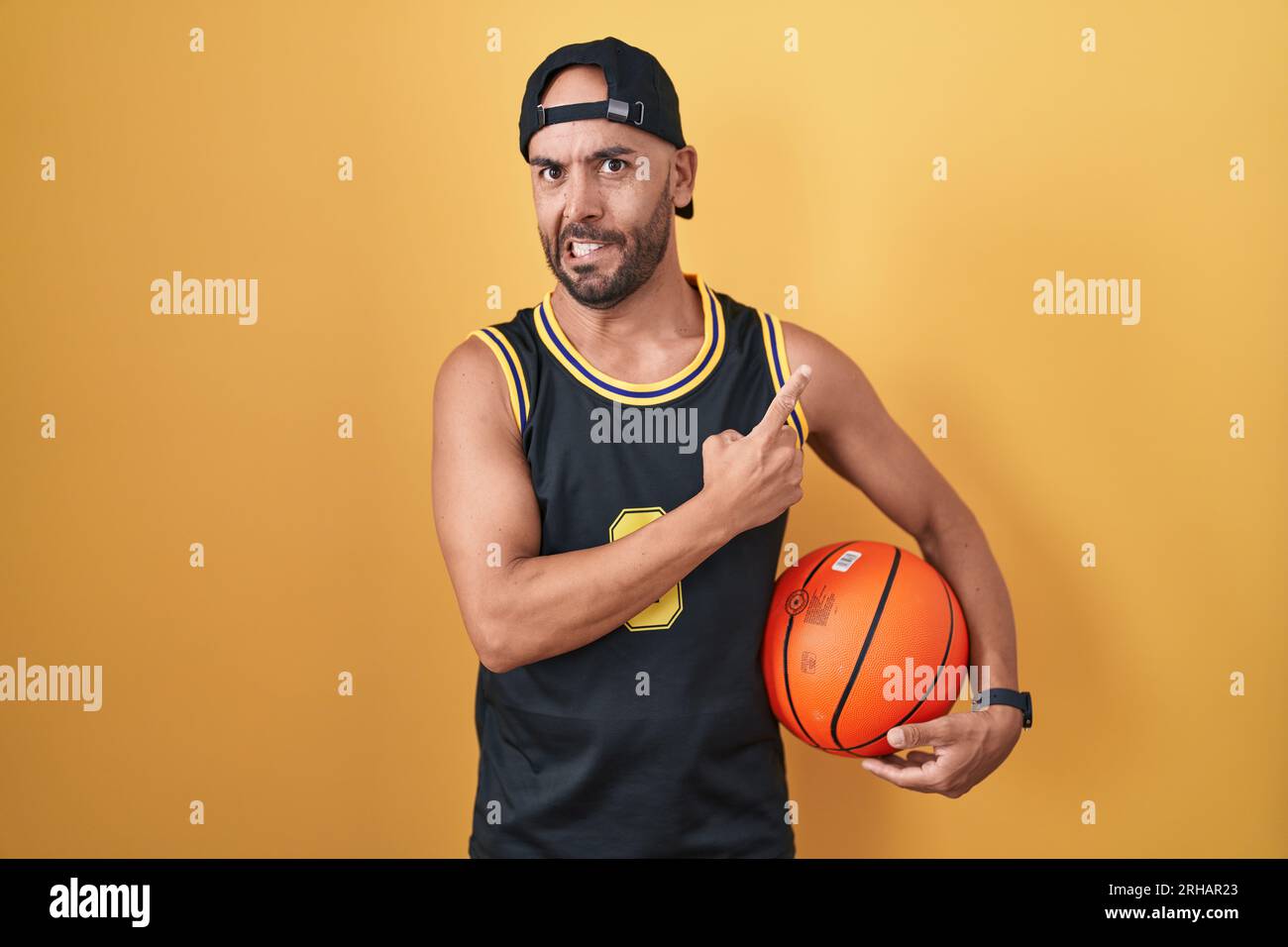 Middle age bald man holding basketball ball over yellow background ...