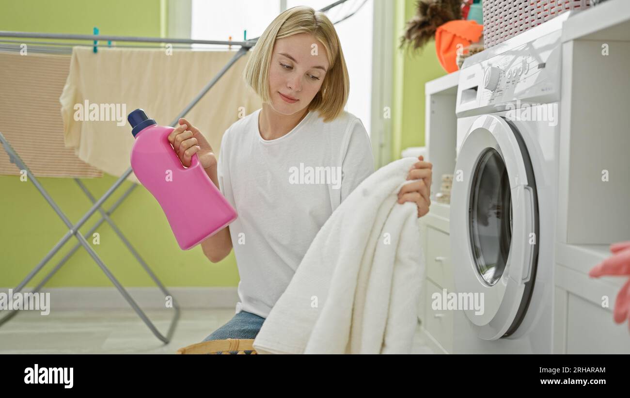 Young blonde woman holding clean towel and detergent bottle at laundry room Stock Photo - Alamy