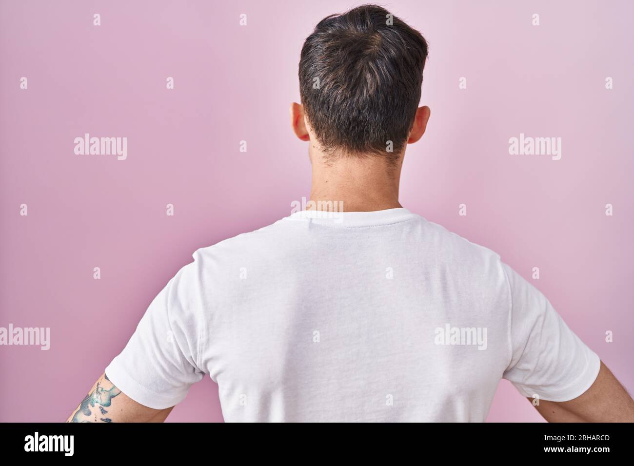 Caucasian man standing over pink background standing backwards looking ...