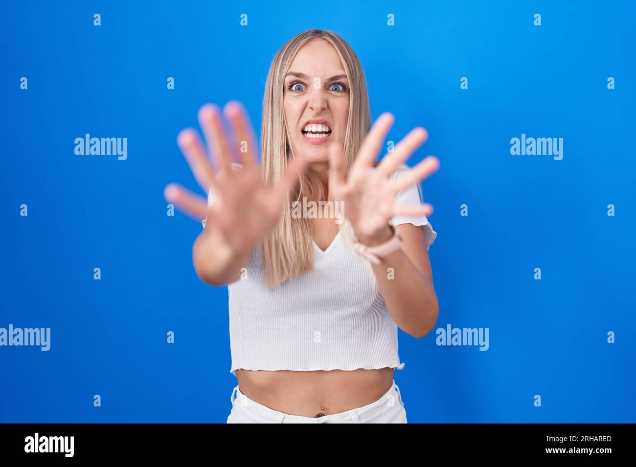 Young caucasian woman standing over blue background afraid and ...