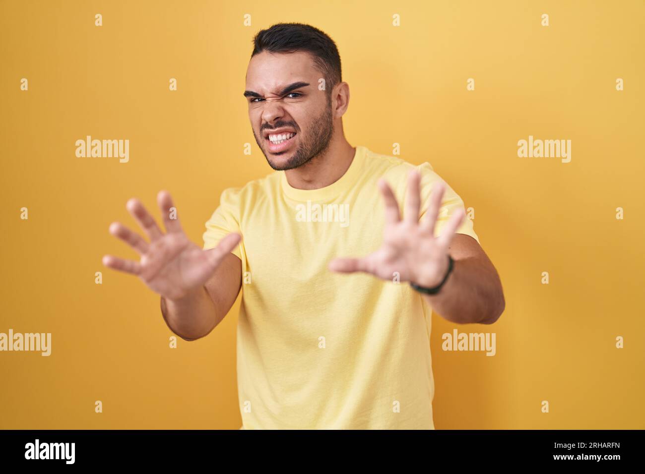 Young hispanic man standing over yellow background afraid and terrified ...