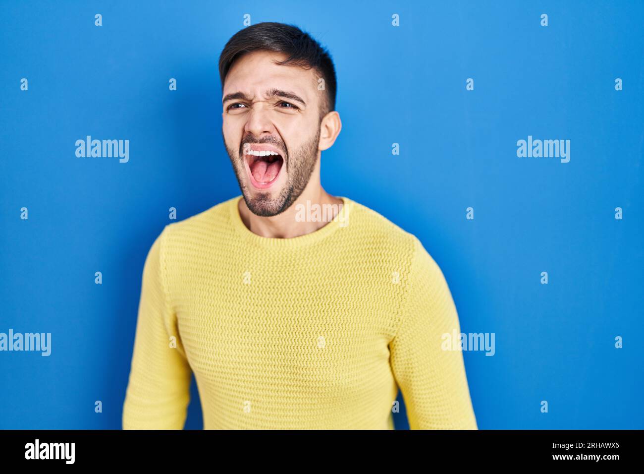 Hispanic man standing over blue background angry and mad screaming ...
