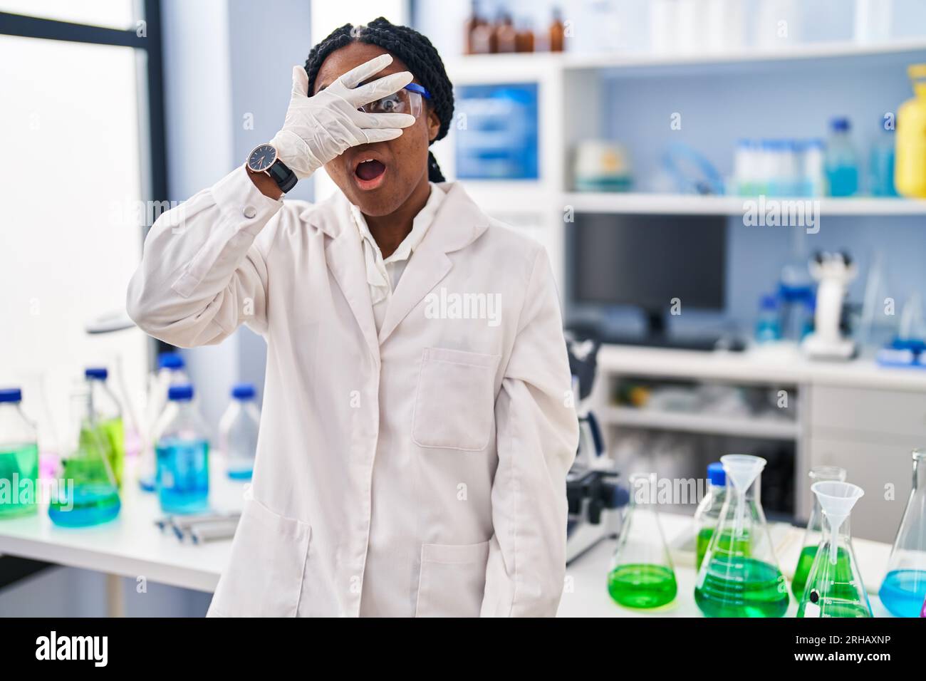 African american woman working at scientist laboratory peeking in shock ...