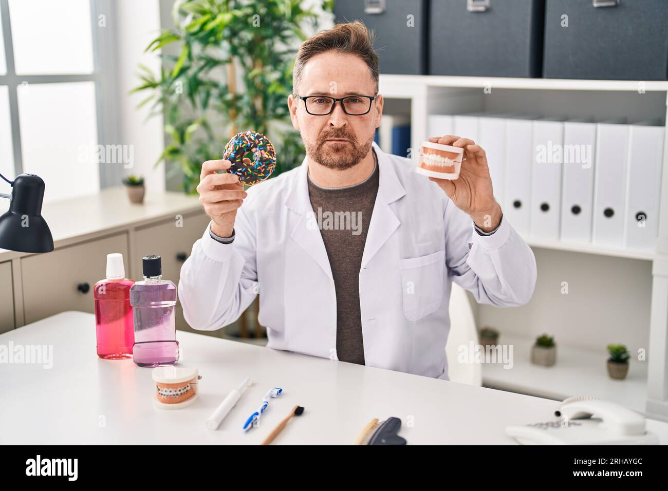 Middle age caucasian dentist man holding denture and doughnuts ...