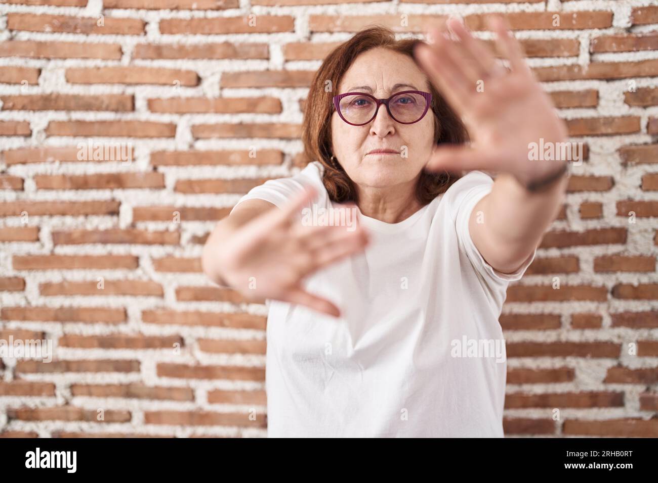 Senior woman with glasses standing over bricks wall doing frame using ...