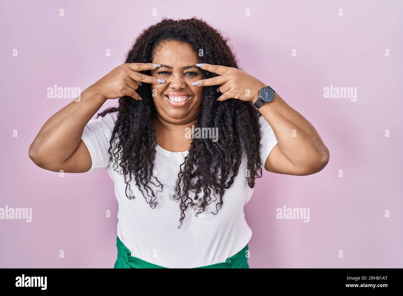 Plus size hispanic woman standing over pink background doing peace ...