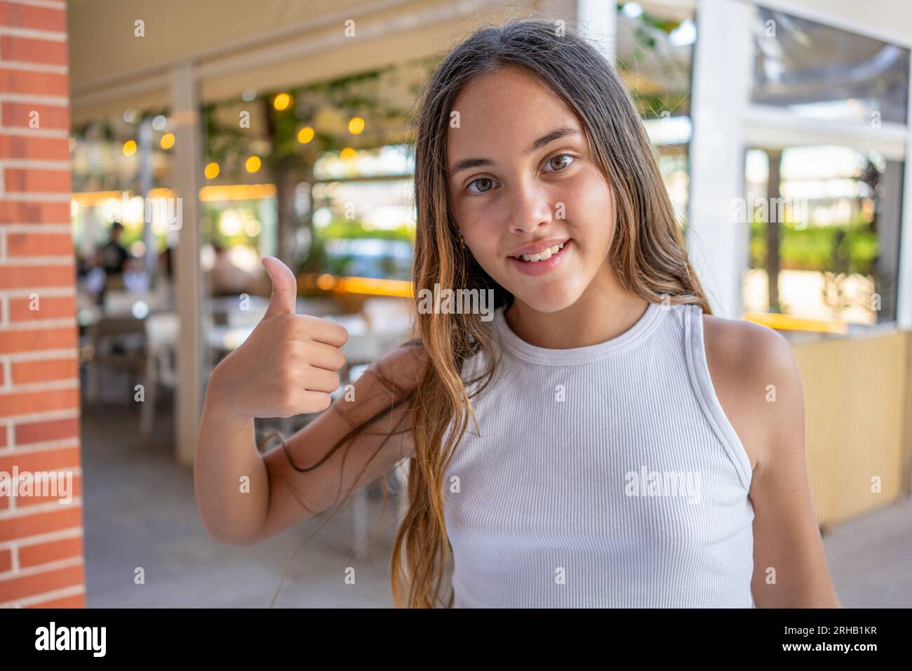 Outdoor portrait of 12 years old girl with long hair showing thumb up ...