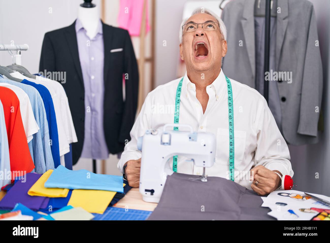 Middle age man with grey hair dressmaker using sewing machine angry and ...
