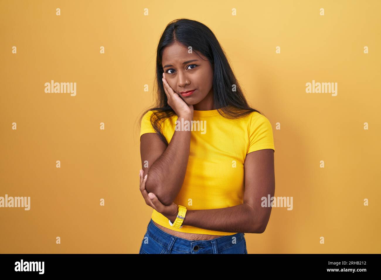Young indian woman standing over yellow background thinking looking ...