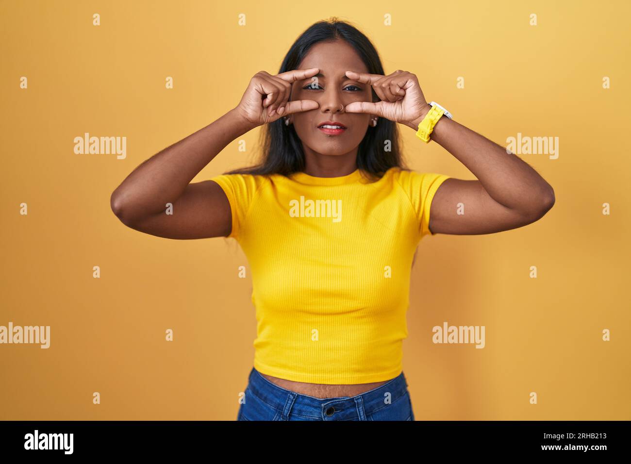 Young indian woman standing over yellow background trying to open eyes ...