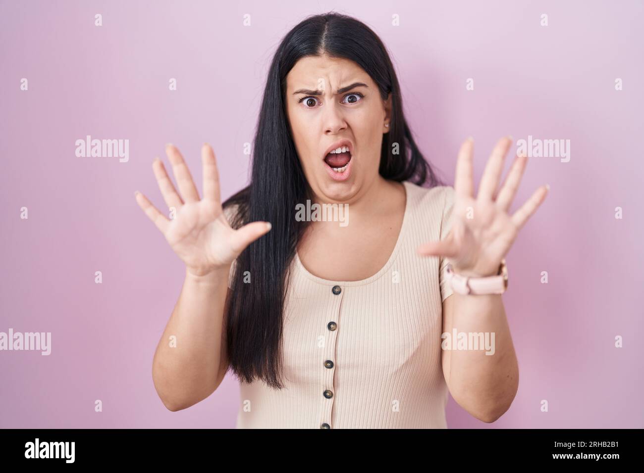 Young hispanic woman standing over pink background afraid and terrified ...