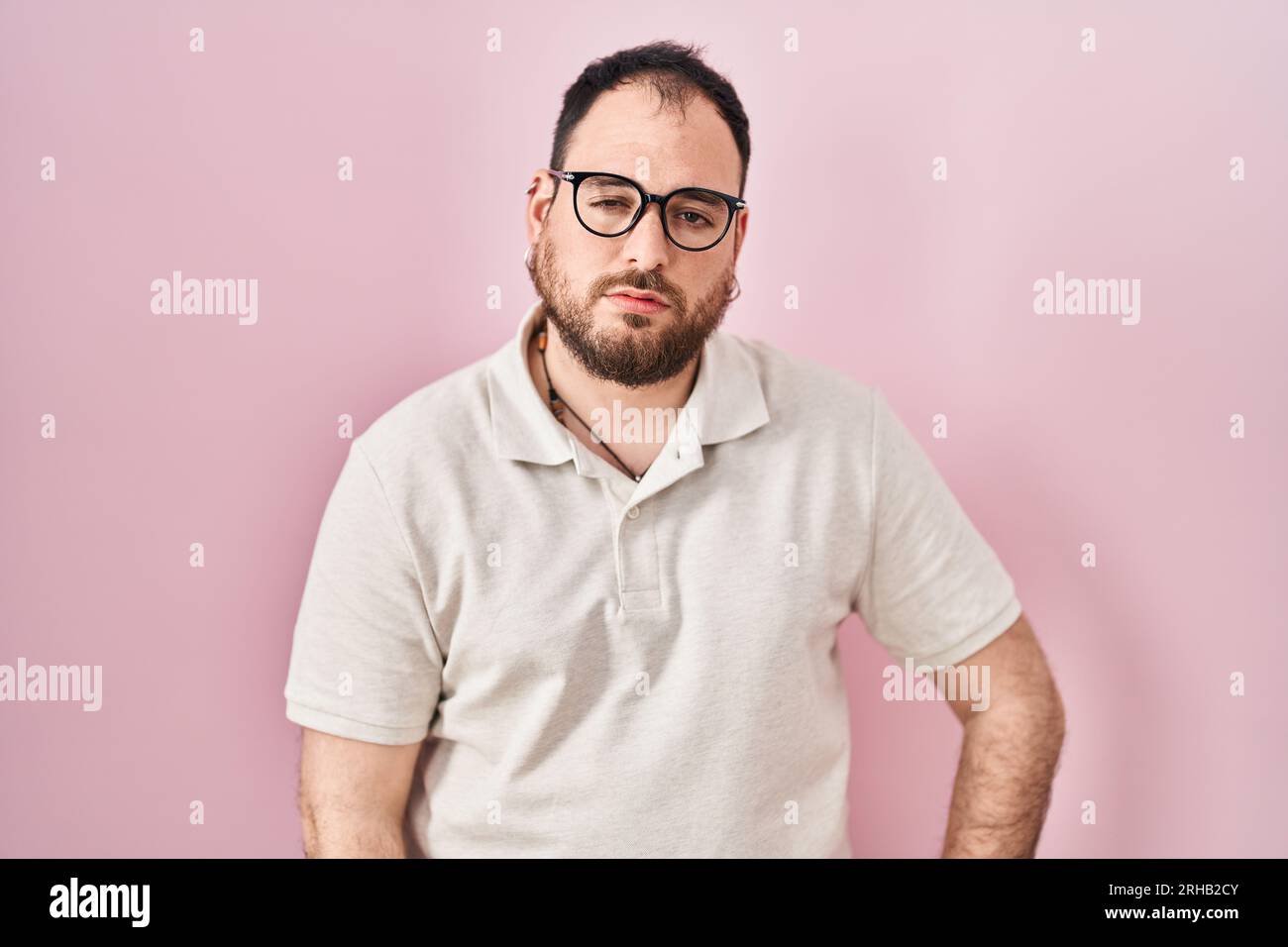 Plus size hispanic man with beard standing over pink background looking ...