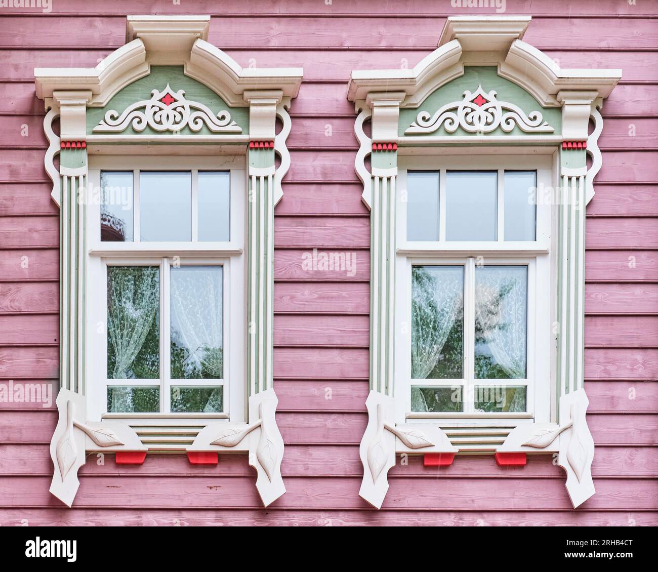 Typical two wooden windows with carved architraves on pink boardwalk ...