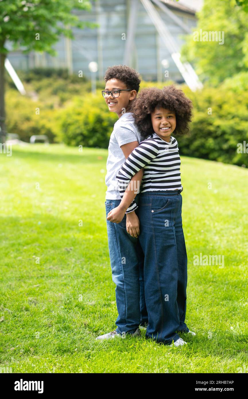 Boy and girl having fun in park standing back to back playing outdoor ...