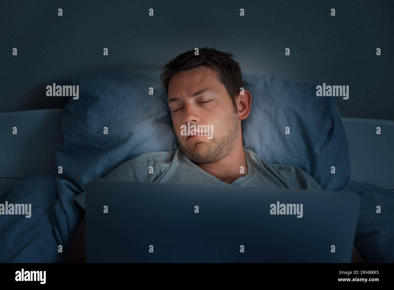 Young man sleeping in front of a laptop in a bed at home, tired after ...