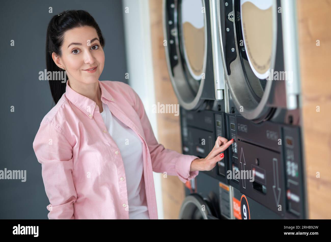 Young woman pressing button in washing machine at public laundry Stock ...