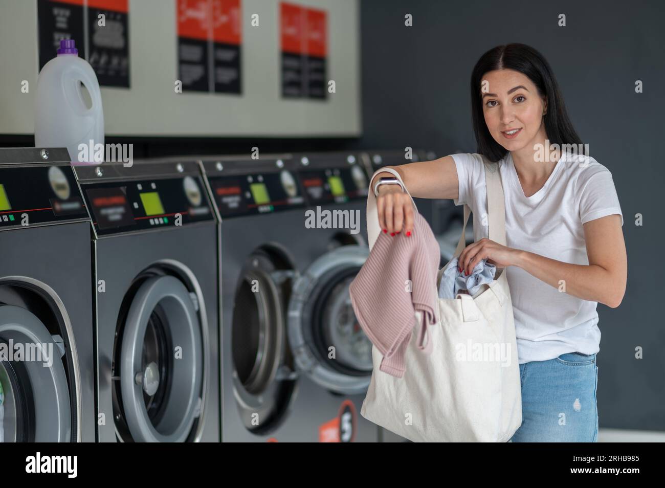 Woman unloading clothes into the washing machine in the laundry room ...