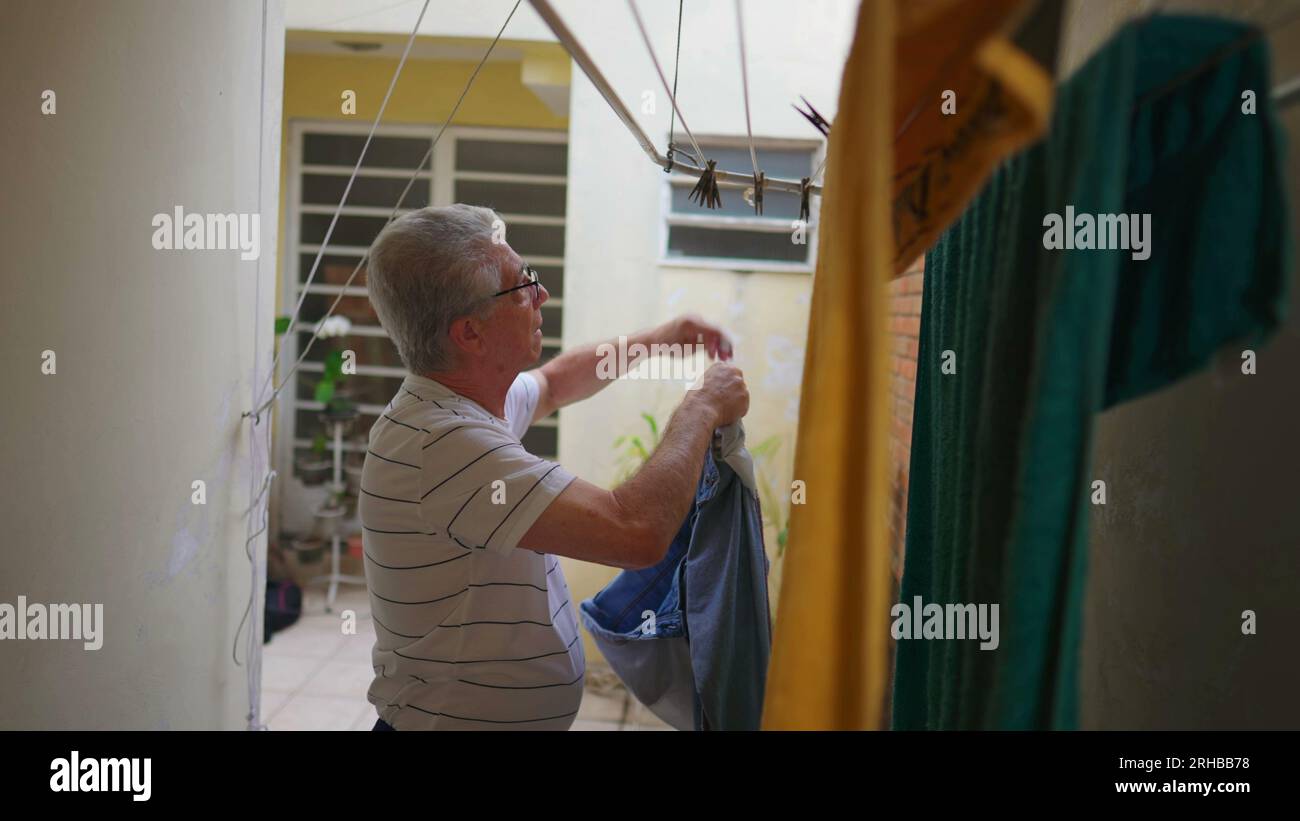 Senior man doing domestic household chores activities, removing clothes ...