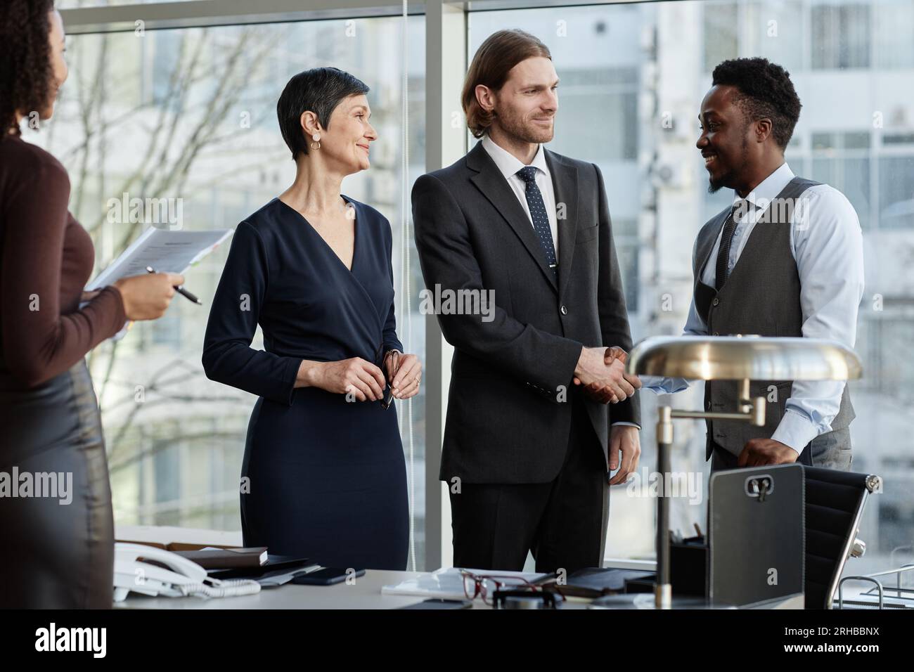 Multiethnic group of smiling business partners shaking hands in office ...