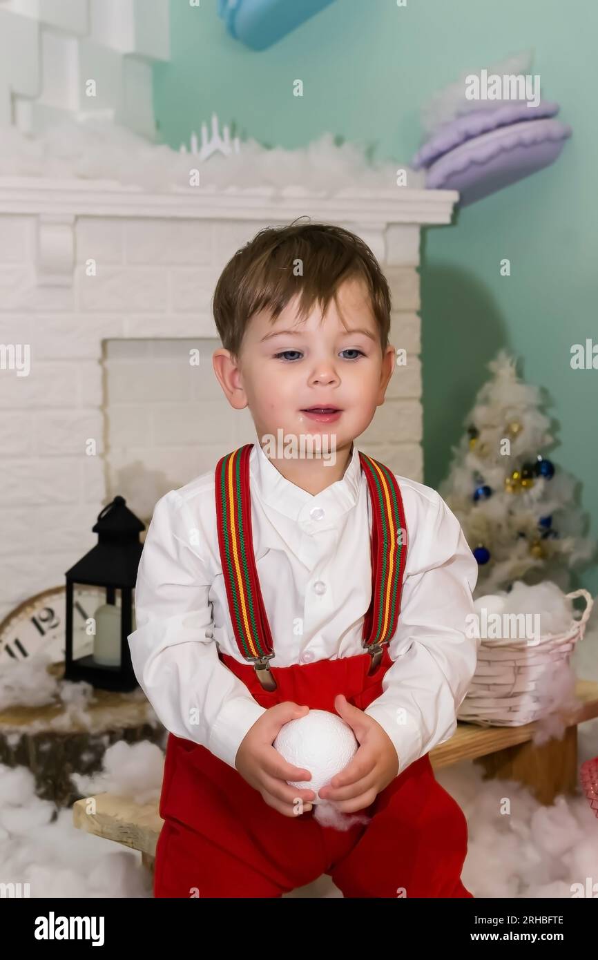 A little boy in red clothes have fun in the artificial snow by the ...