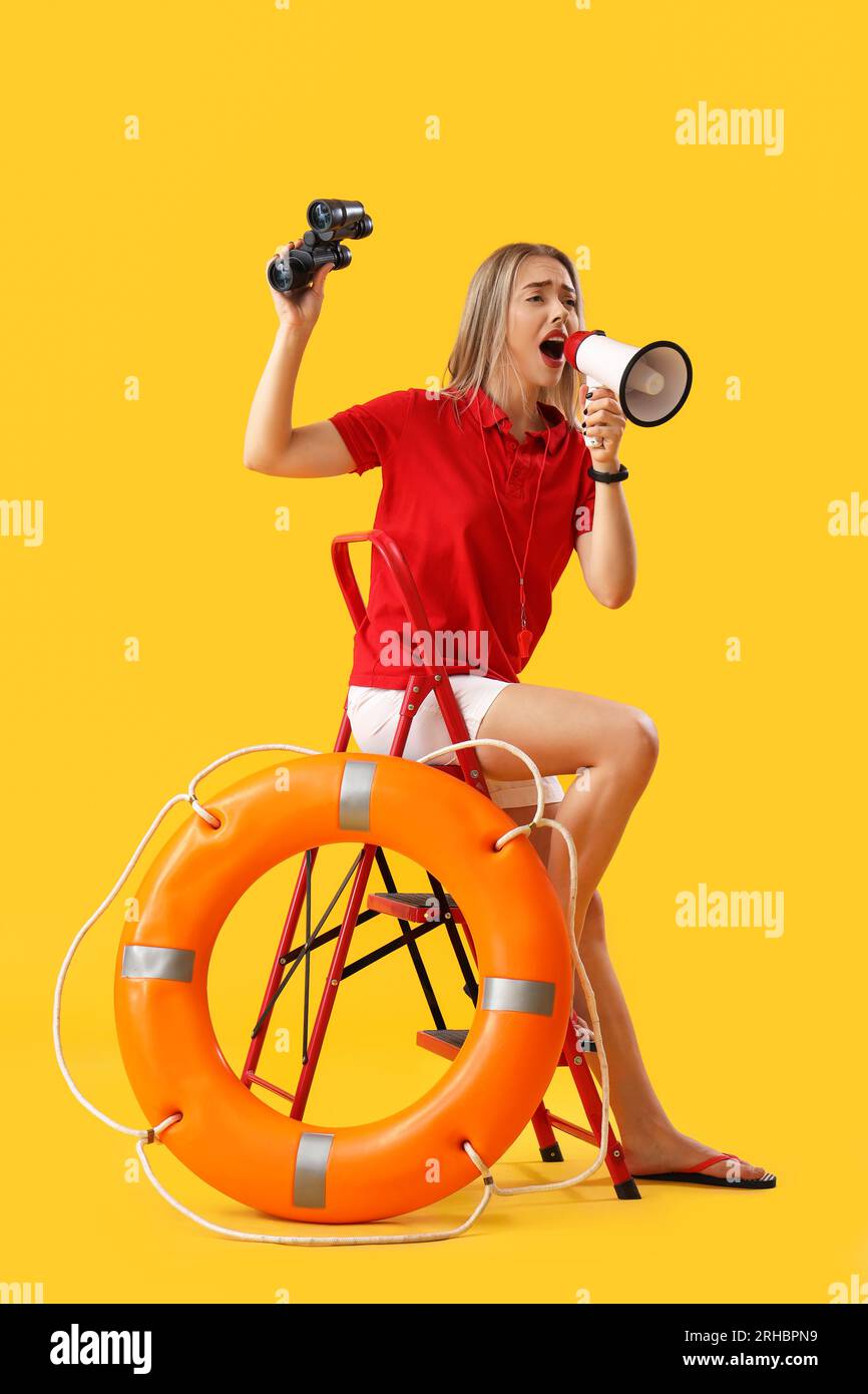 Female lifeguard with binoculars and ring buoy shouting into megaphone ...